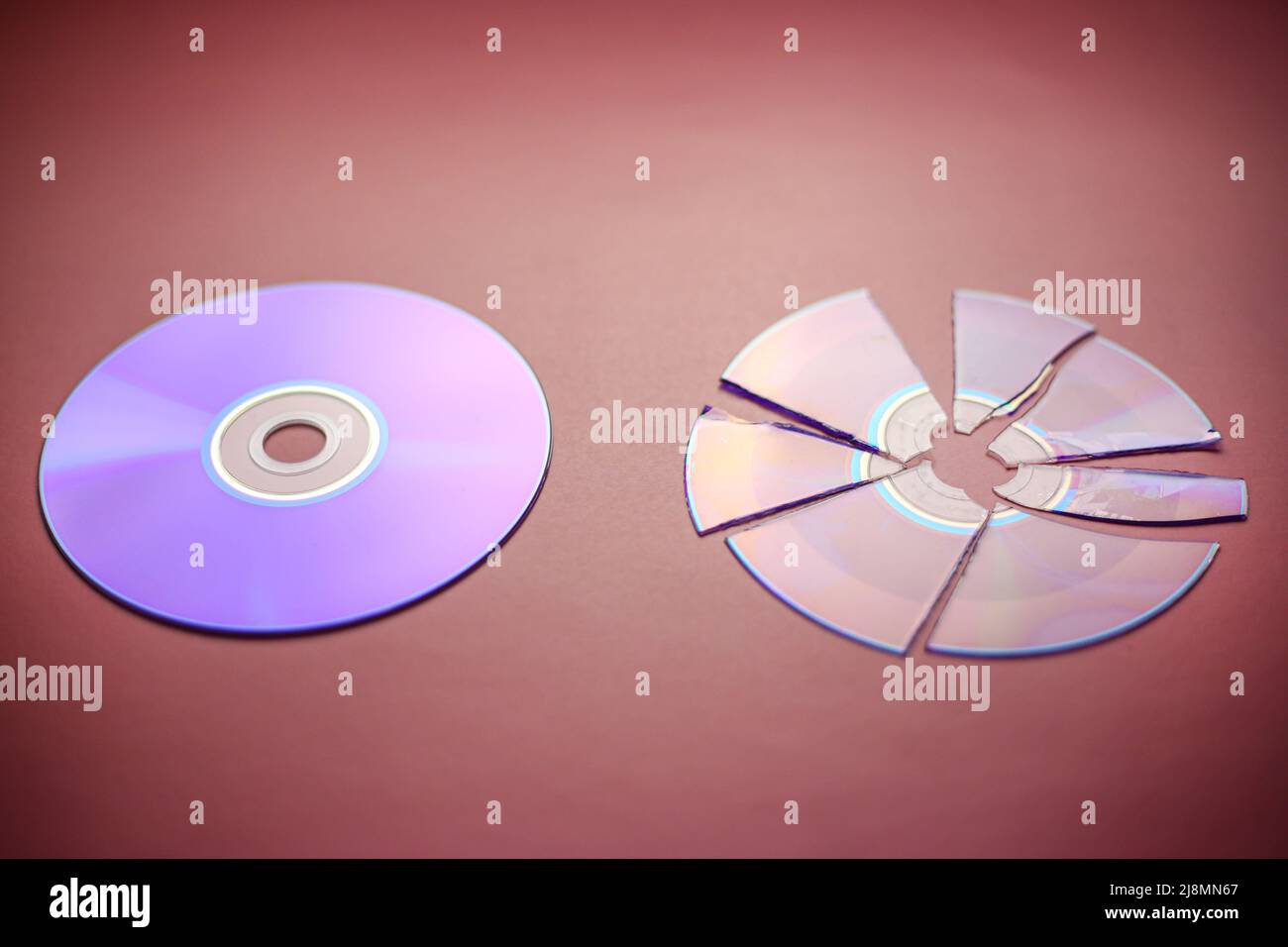 Broken compact disc divided into parts and a whole compact disc close ...