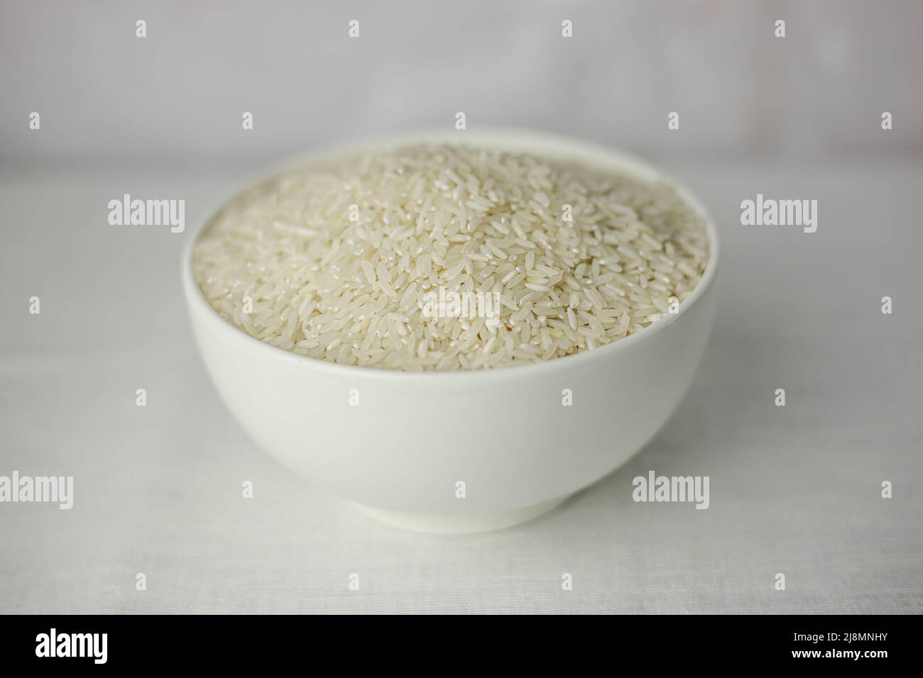 Rice in a white deep plate close-up side view on a white textured ...