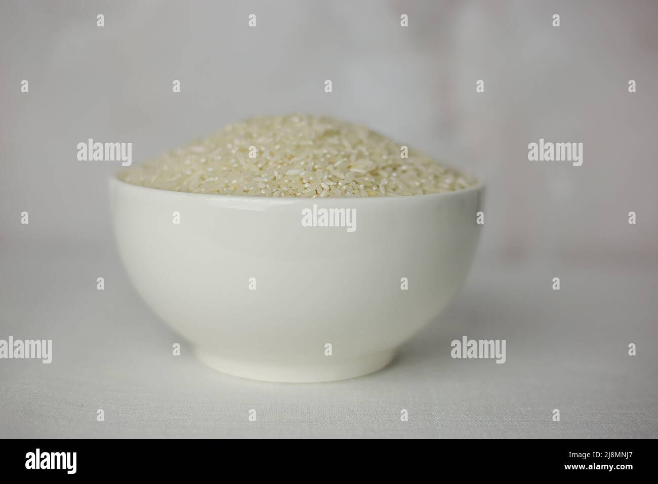 Rice in a white deep plate close-up side view on a white textured ...