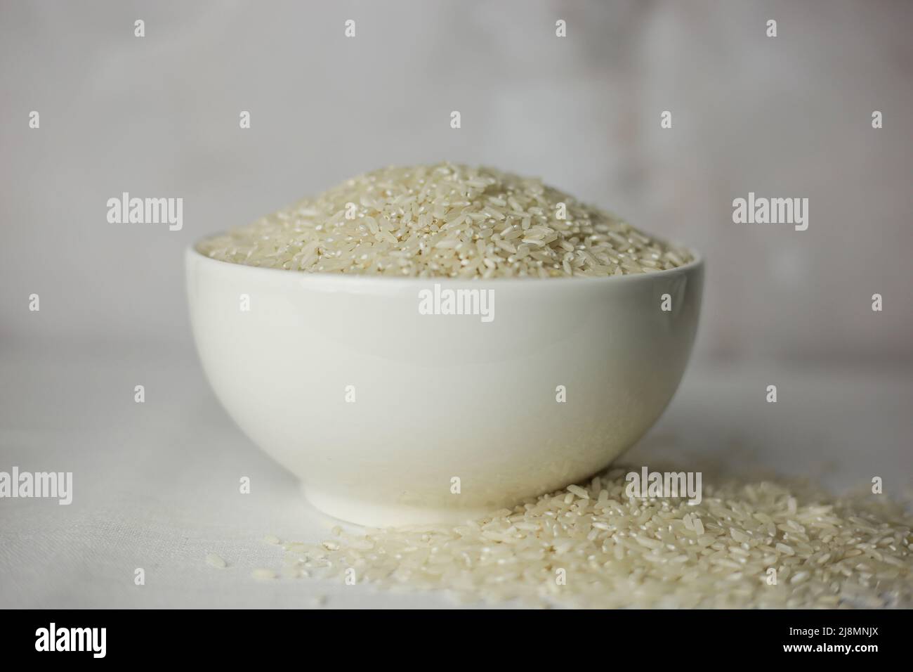 Rice in a white deep plate close-up side view on a white textured ...