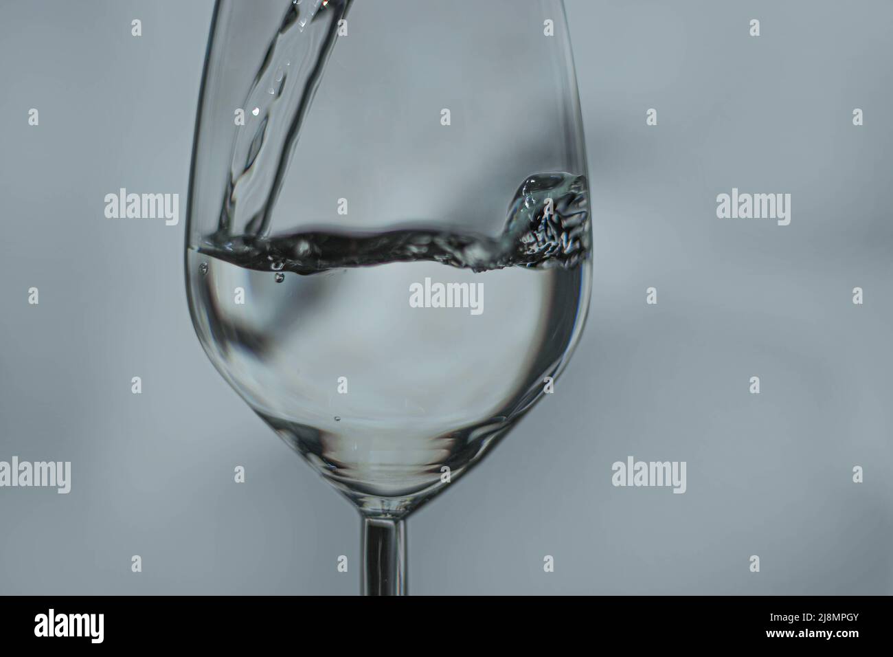 A stream of clean water is poured into a glass from a bottle close-up on a light, gray ...