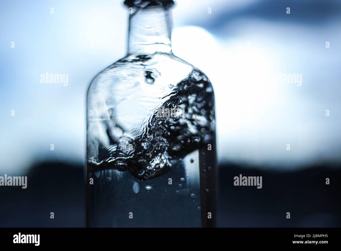 A splash of water in a bottle close-up on a dark, light background ...
