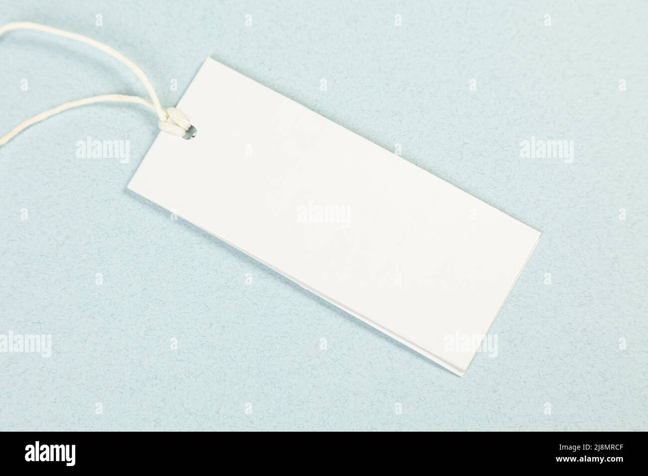 An empty white price tag lies on a gray-blue background with a soft ...