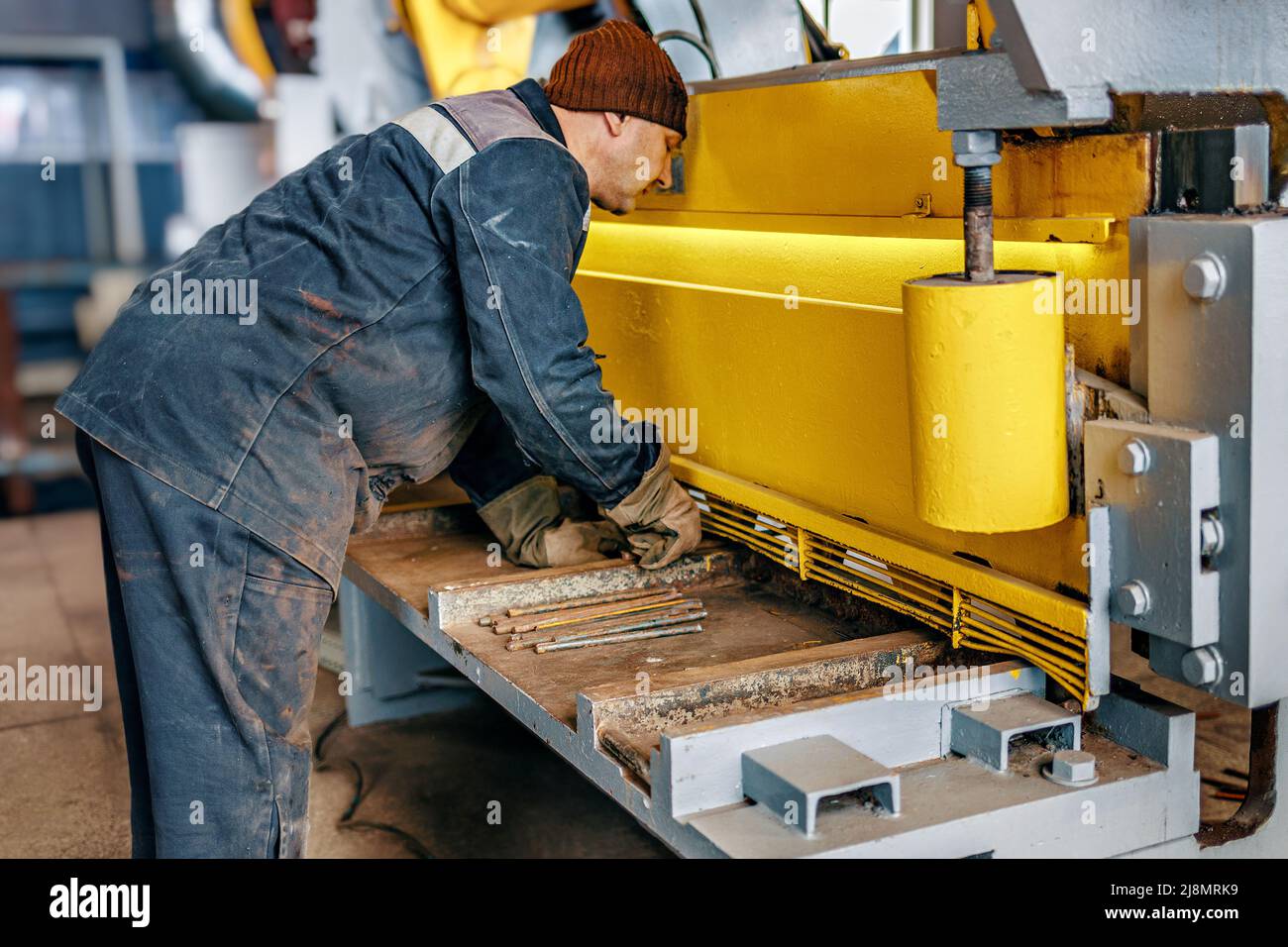 Worker cuts metal on mechanical guillotine machine in production hall ...