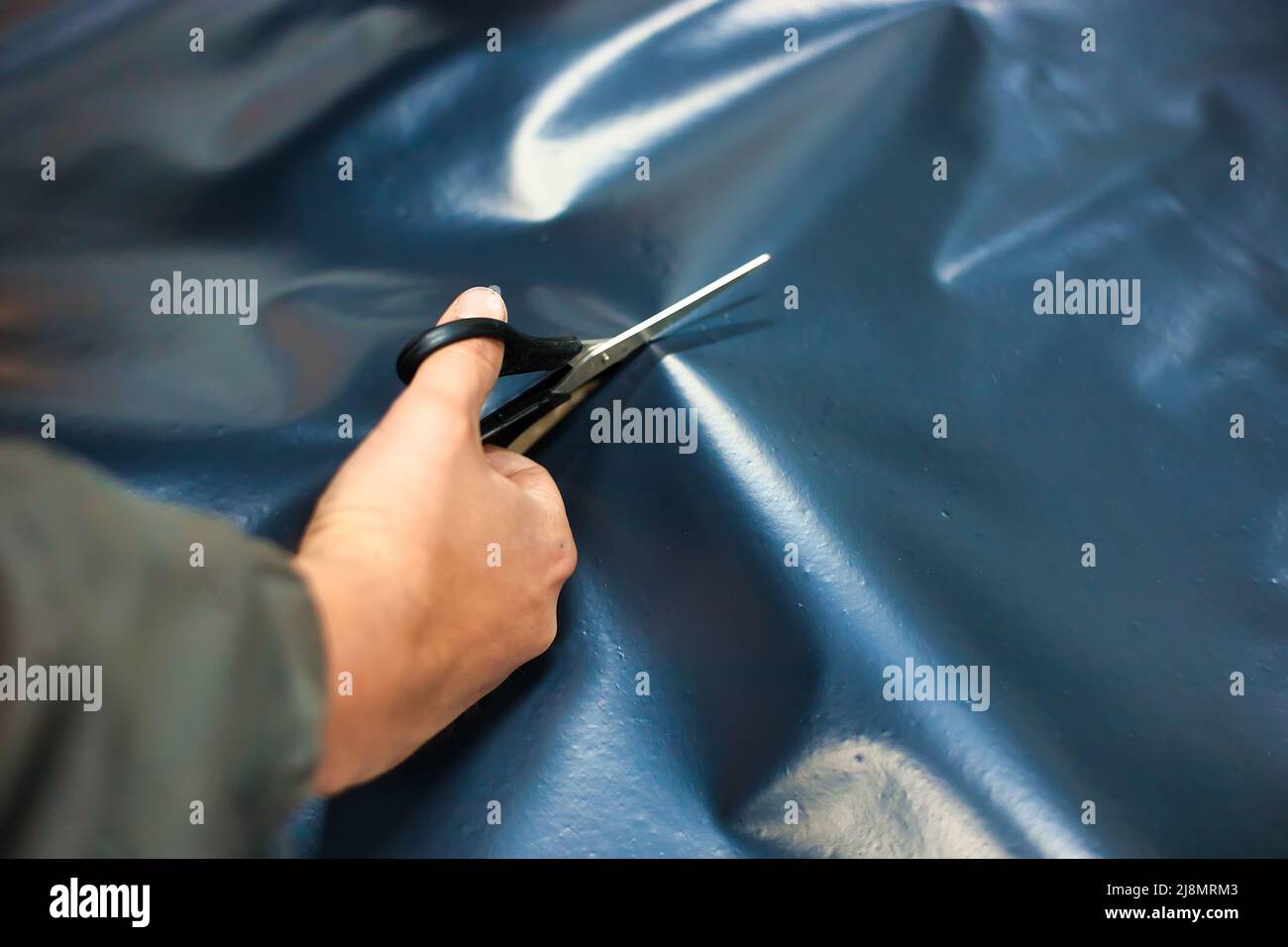 Hand with scissors cuts off gray polyethylene material. Background ...