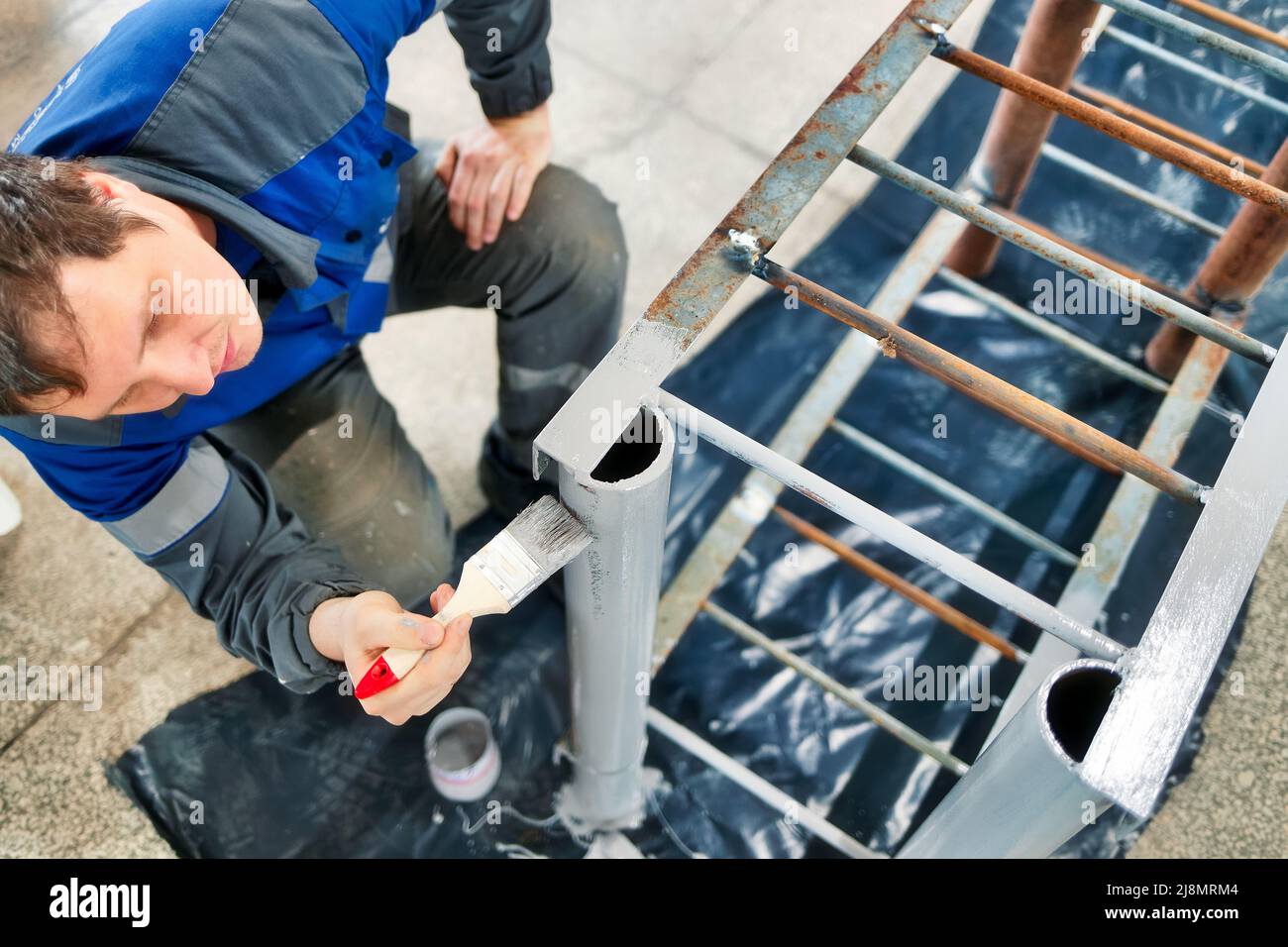 Caucasian worker in overalls paints metal rack or ladder with paint ...