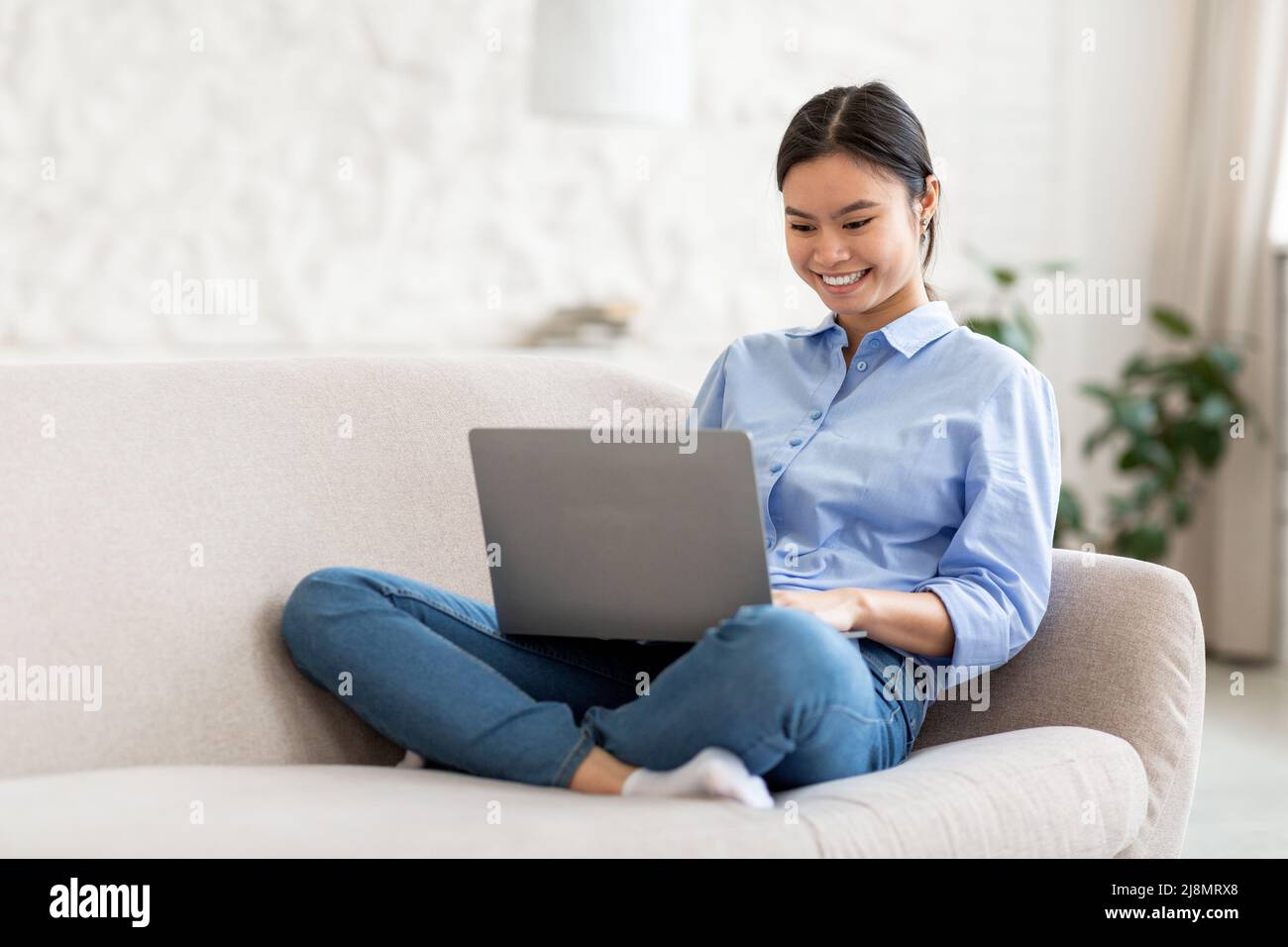 Relaxed asian lady sitting on couch, using laptop Stock Photo - Alamy