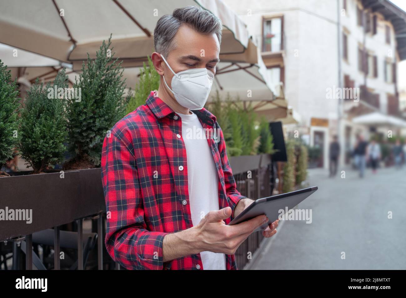 Man looking at tablet standing near cafe Stock Photo - Alamy