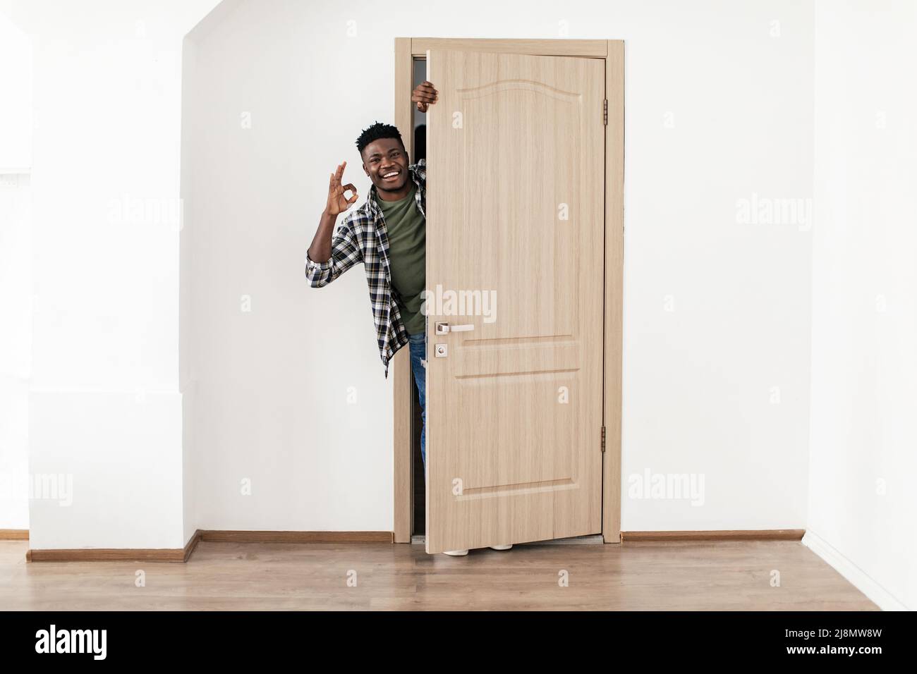 African Guy Gesturing Okay Standing In Opened Door At Home Stock Photo ...