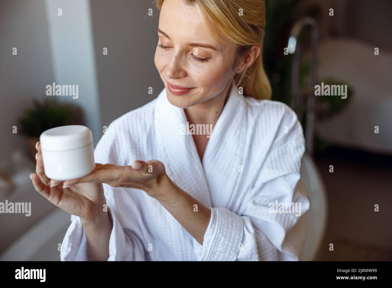 Attractive blonde young female demonstrating facial cream or body ...