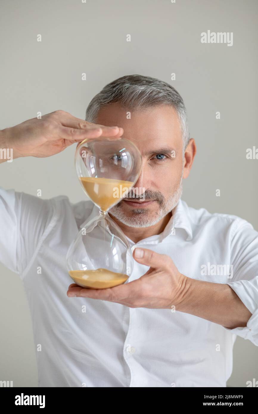 A man in white shirt with a sand watch in hands Stock Photo - Alamy