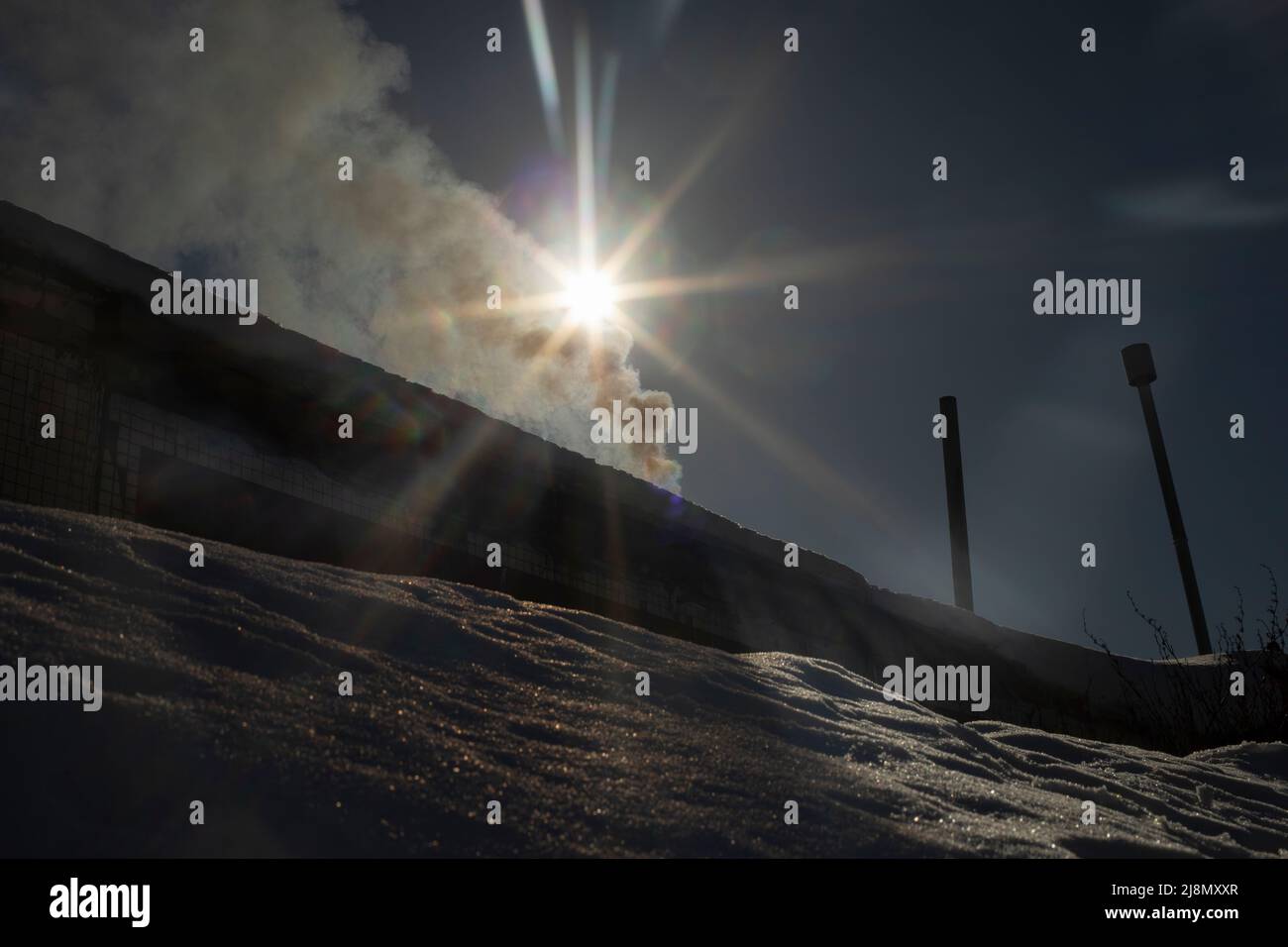 Smoke from chimney in background of sun. Bright rays in sky. View of ...