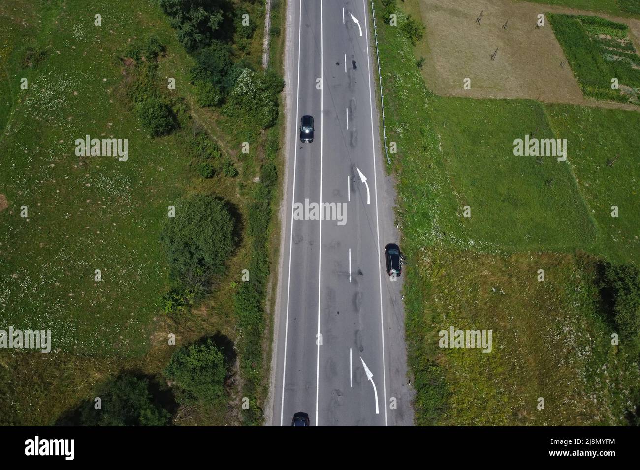 Aerial view from drone of highway with three lanes between green fields ...