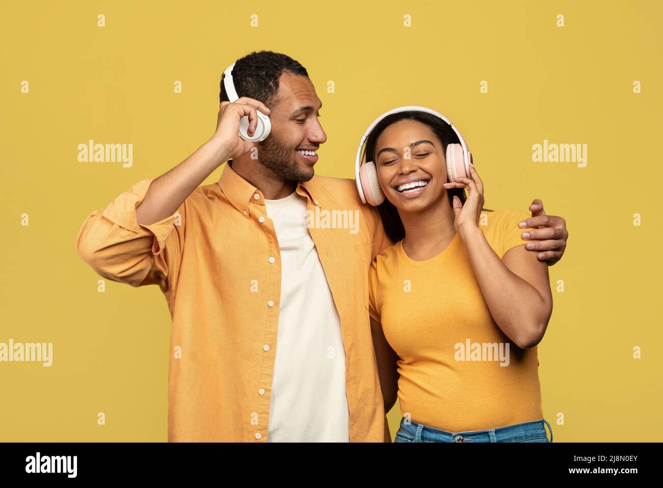 Happy young black couple in wireless headphones listening to music and ...