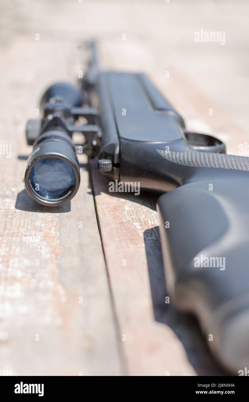 A sniper rifle with an optical sight lies on a worn wooden board ...