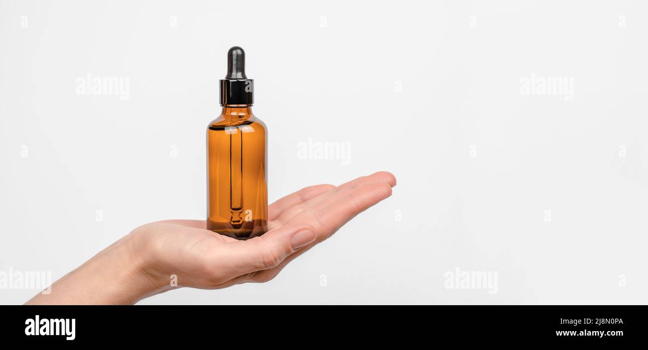 Brown cosmetic bottle in a female hand. A bottle of essential oil or ...