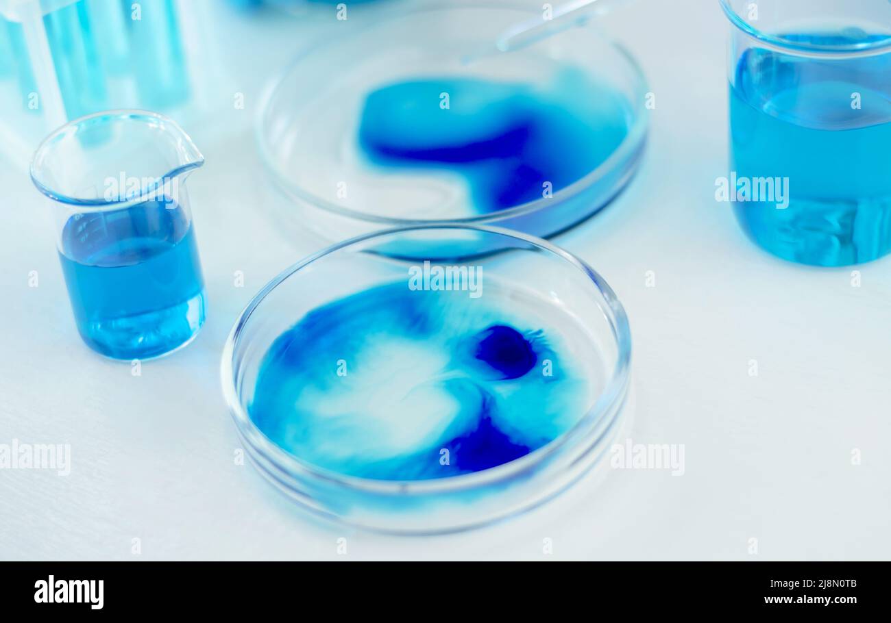 Laboratory glassware with blue and cyan liquid on a white table ...