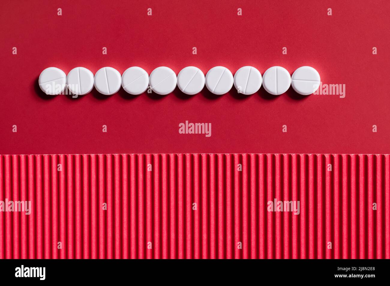 top view of row with white round shape pills on crimson and textured ...