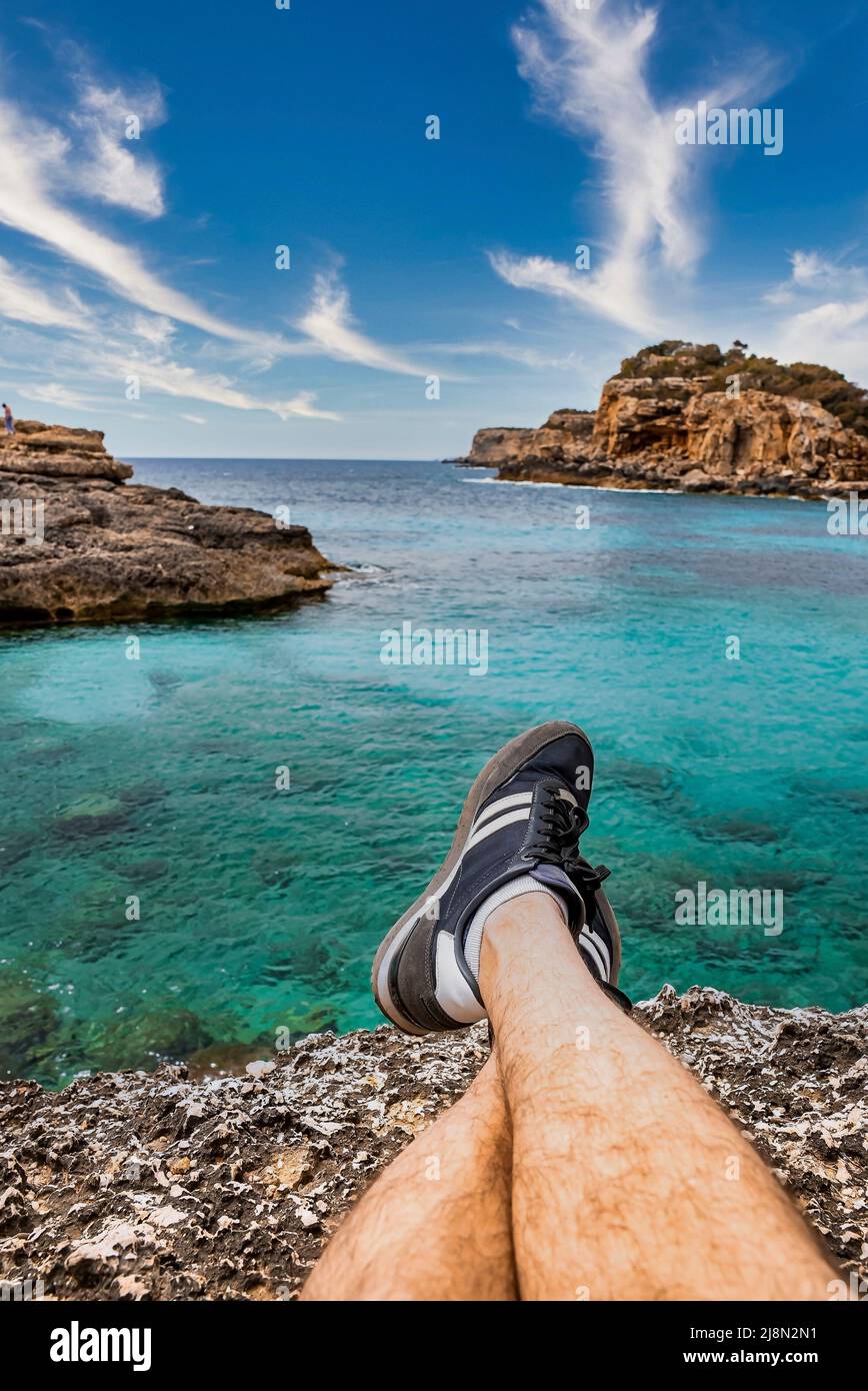 Low section of man wearing shoes relaxing on rock formation overlooking ...