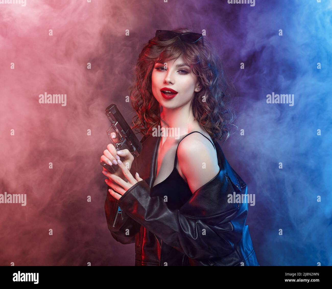 beautiful young Caucasian girl with bright red lips poses with a gun ...