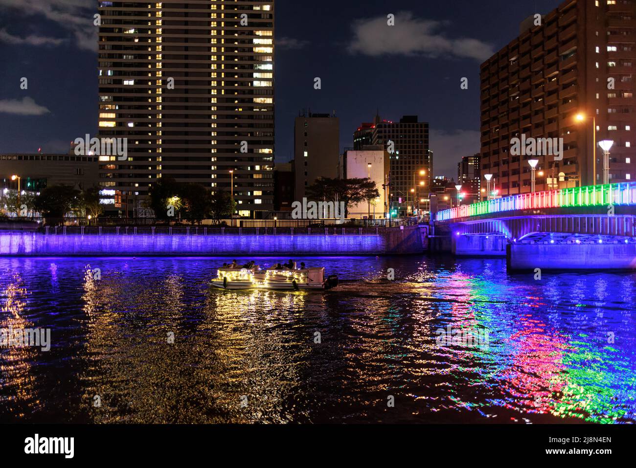 Colorful bridge reflects off ripples in river through city at night ...