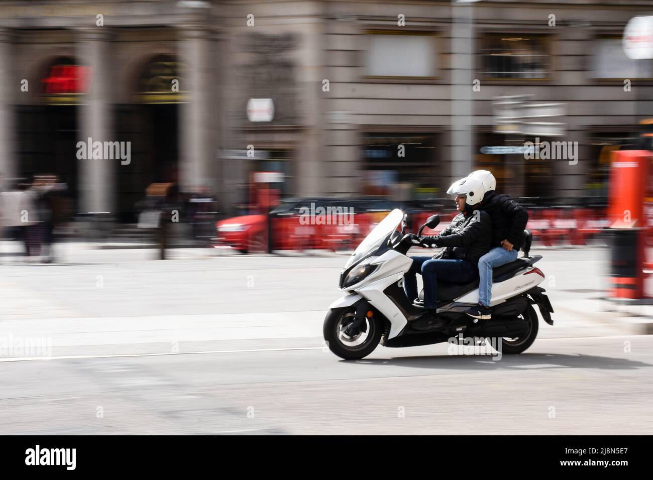 Driver and a passenger driving a motor through the streets of Barcelona ...