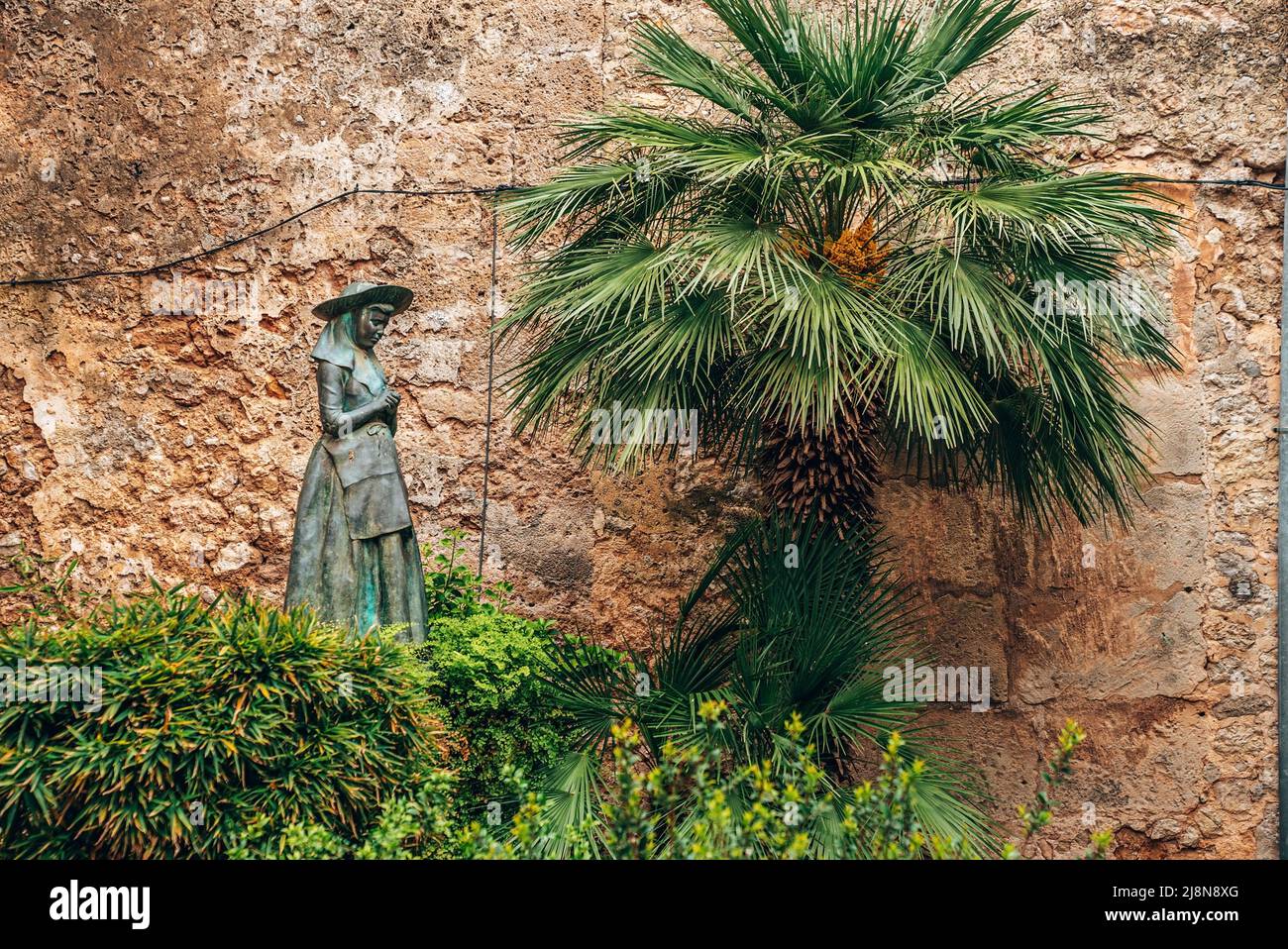 Female statue by palm tree amidst plants against wall in town Stock ...