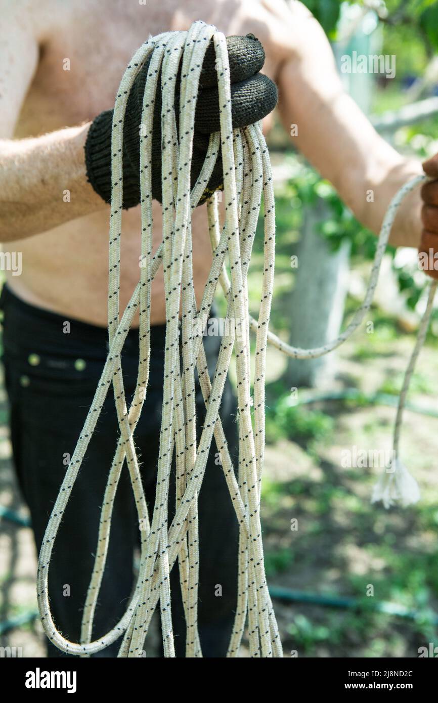 A man of mature years on a personal plot winds a rope for construction ...