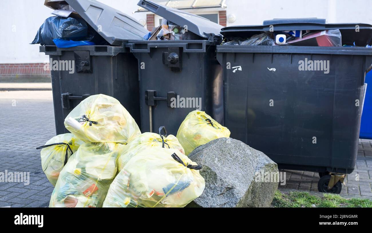 Overflowing plastic garbage containers and waste package lie on a city ...