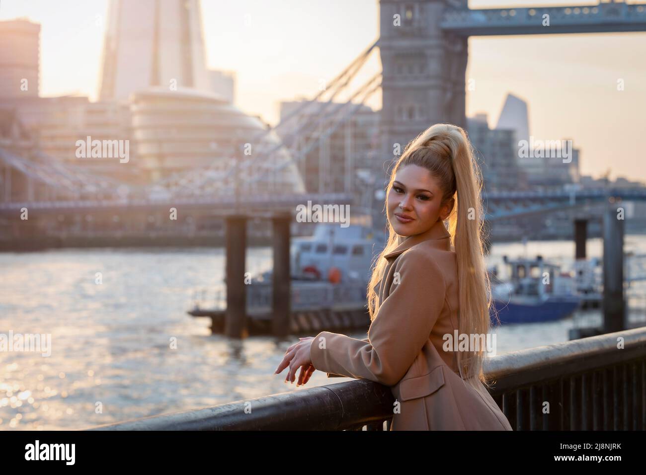 A Blonde Woman In A Coat Stands In Front Of The Skyline Of London Stock
