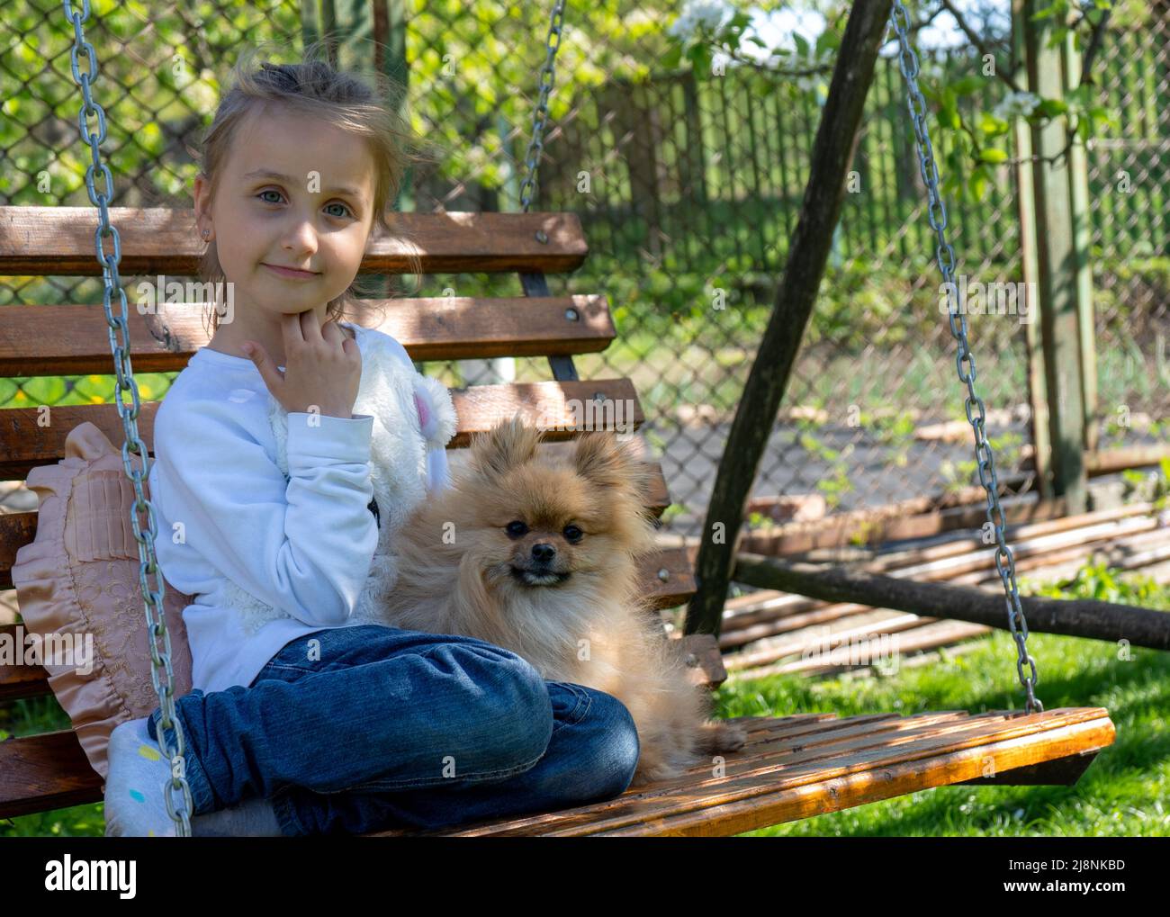 Beautiful little girl sits on a swing in spring, smiles and hugs her ...