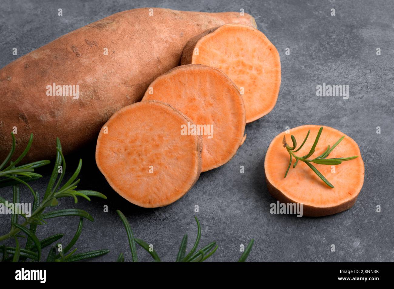 Raw whole orange sweet potato and slices of batatas with fresh rosemary ...