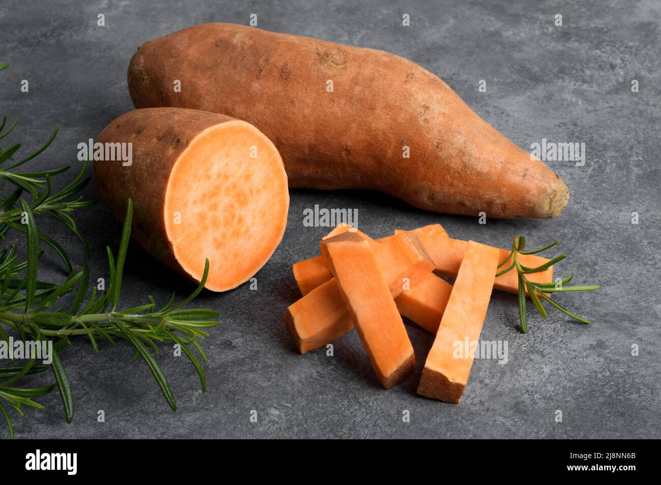 Raw whole orange sweet potato and slices of batatas with fresh rosemary ...