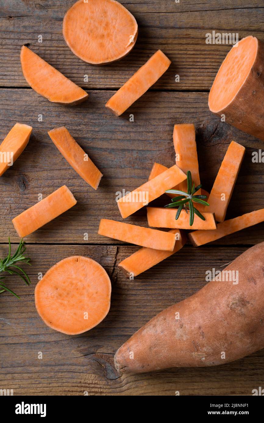 Raw whole orange sweet potato and slices of batatas with fresh rosemary ...