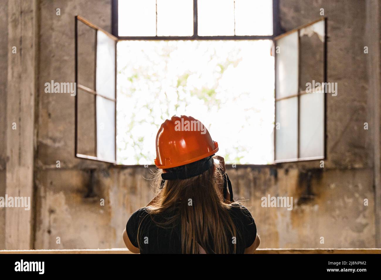Woman in orange helmet on head standing in front of open window of old ...