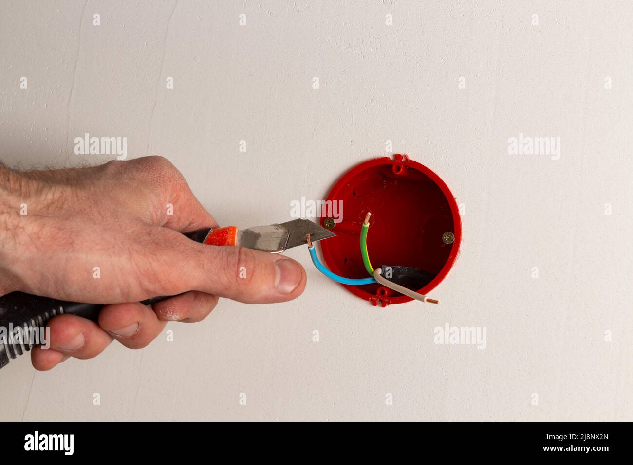 A hand with a knife removes the insulation of wires in a junction box ...