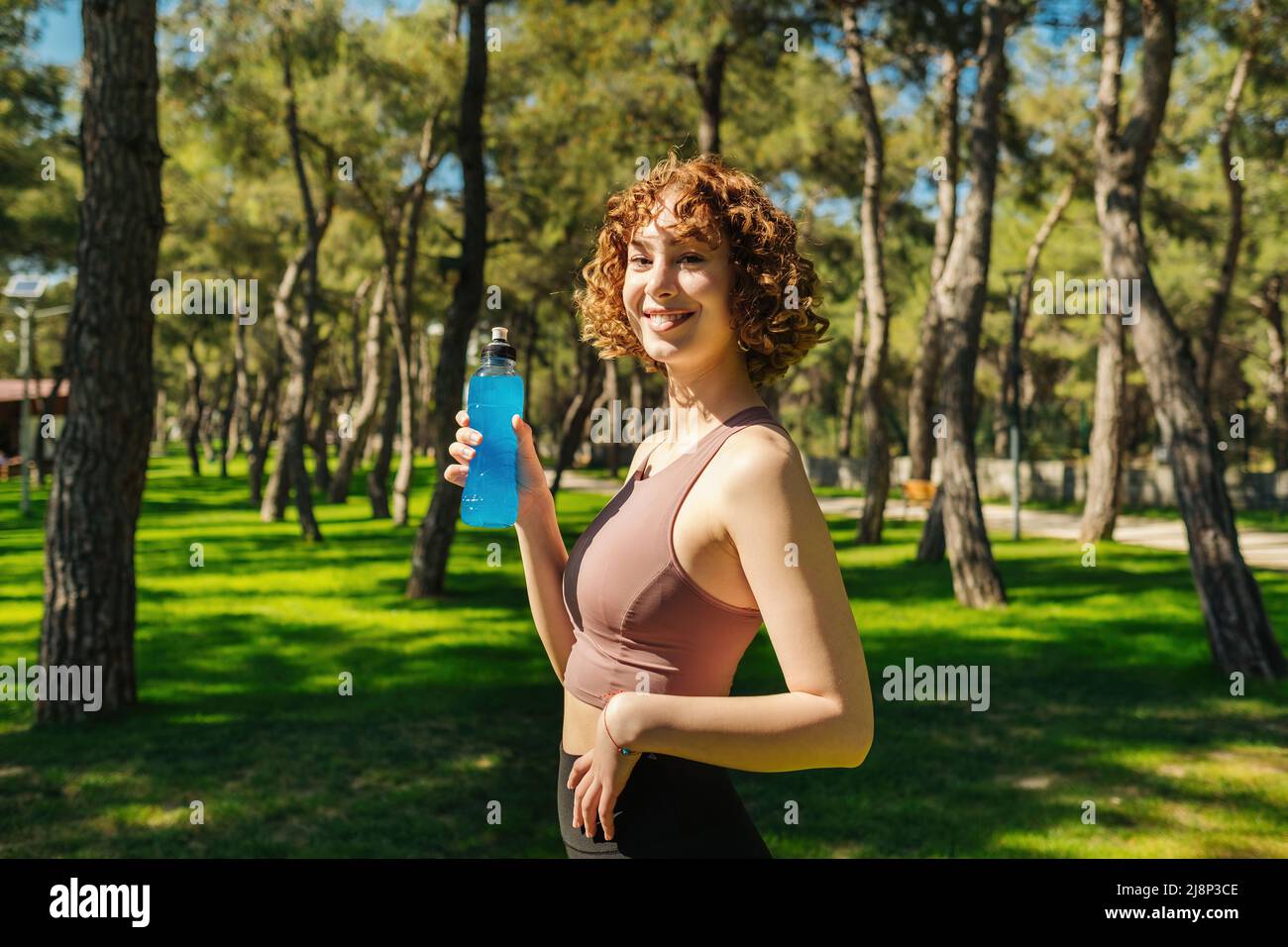 Beautiful happy redhead woman wearing sport bra holding a bottle of ...