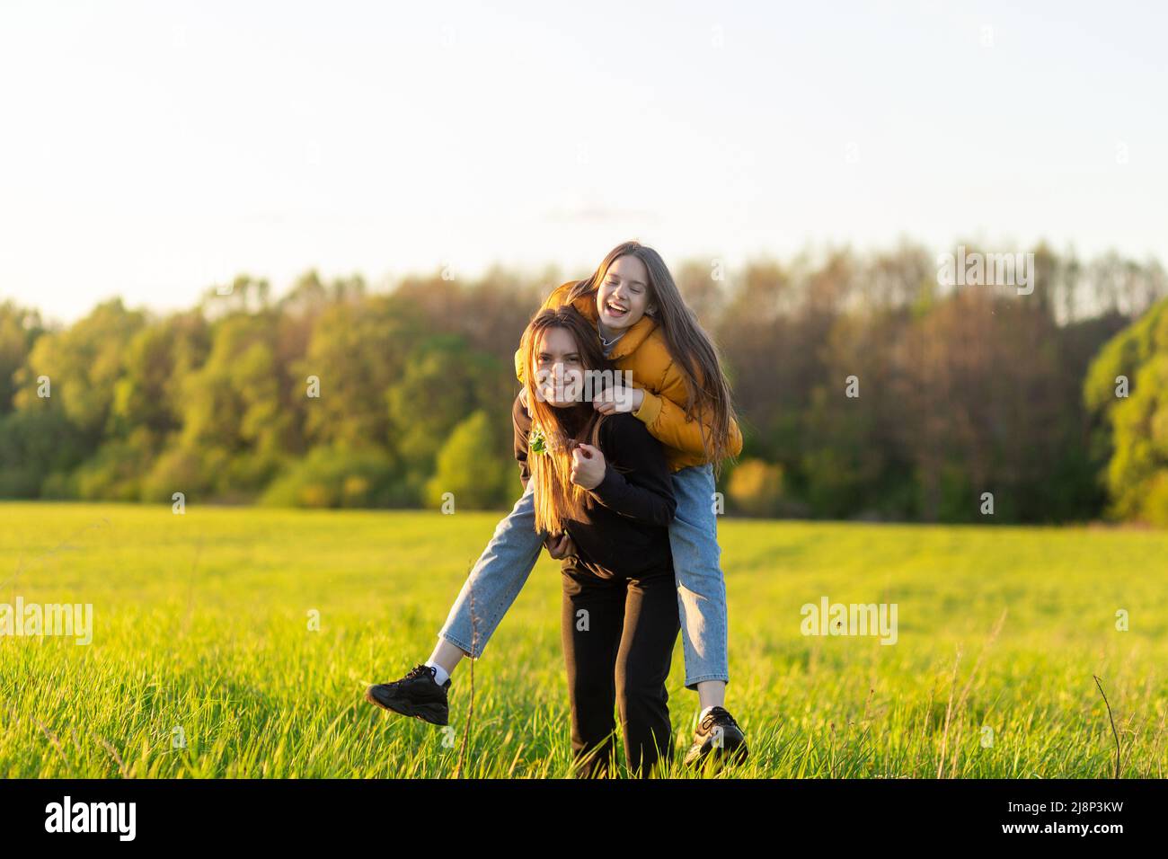Playful mother giving daughter piggy back ride at green field. Both ...