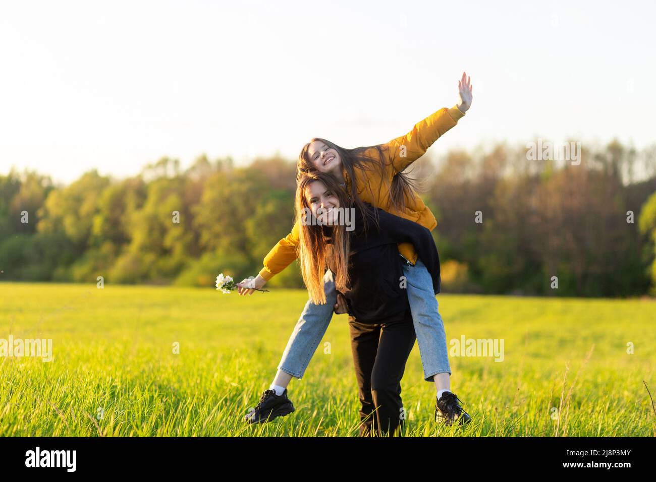 Playful mother giving daughter piggy back ride at green field. Both ...