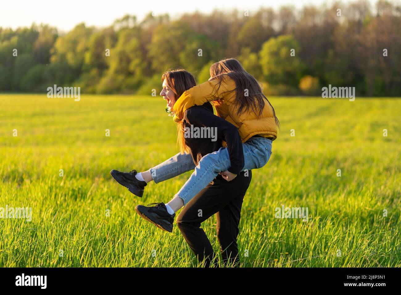 Playful mother giving daughter piggy back ride at green field. Both ...