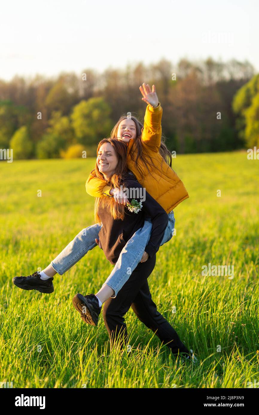 Playful mother giving daughter piggy back ride at green field. Both ...