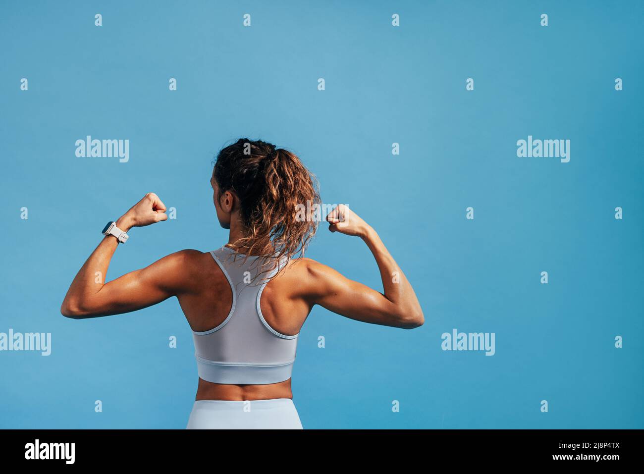 Rear view of young woman showing her biceps on blue background with a ...