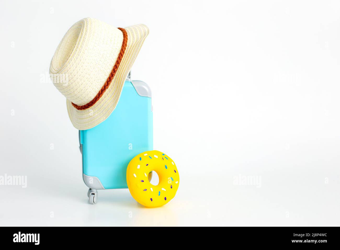 A blue suitcase on wheels, a straw hat, and a yellow inflatable donut ...