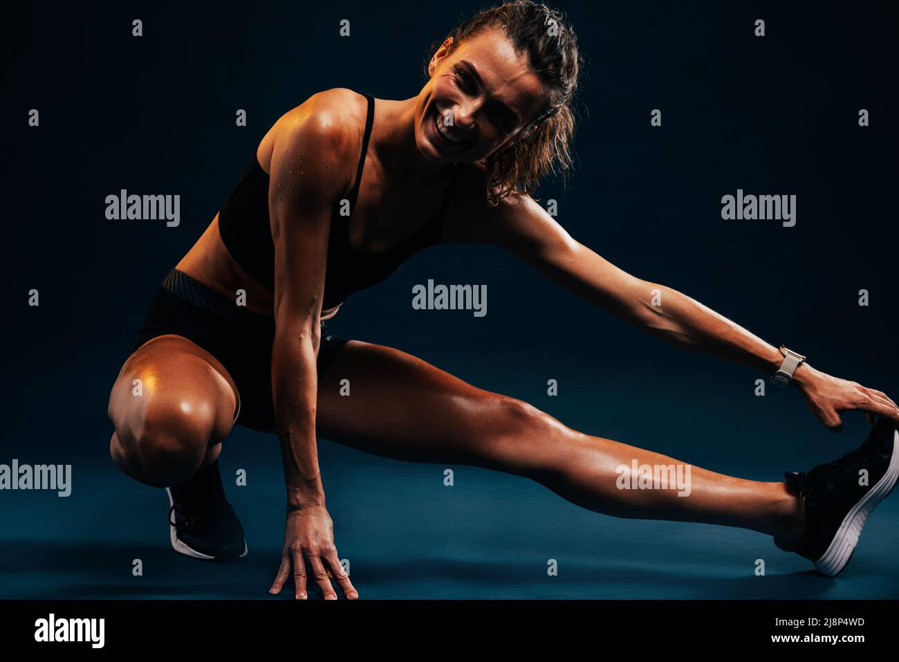 Woman runner stretching her leg and smiling on black background Stock ...