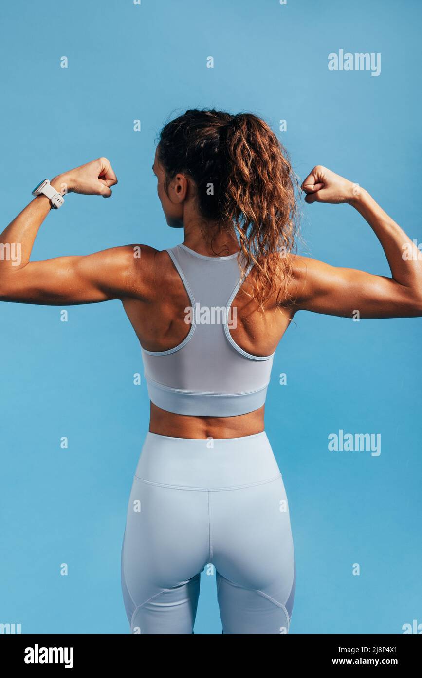 Rear view of muscular fitness woman on blue background. Strong female ...