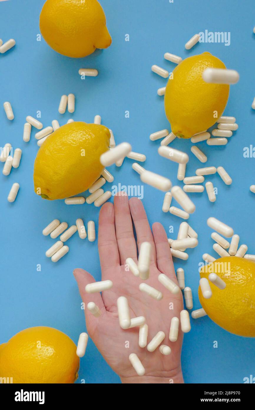 capsules of vitamin C in a hand and yellow citrus fruits on a blue ...