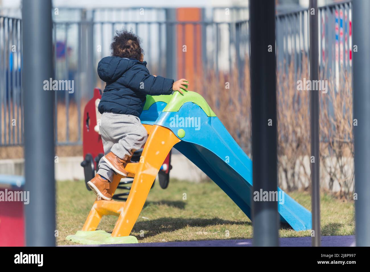 Little biracial boy climbing on the playground slide. Child curiosity ...