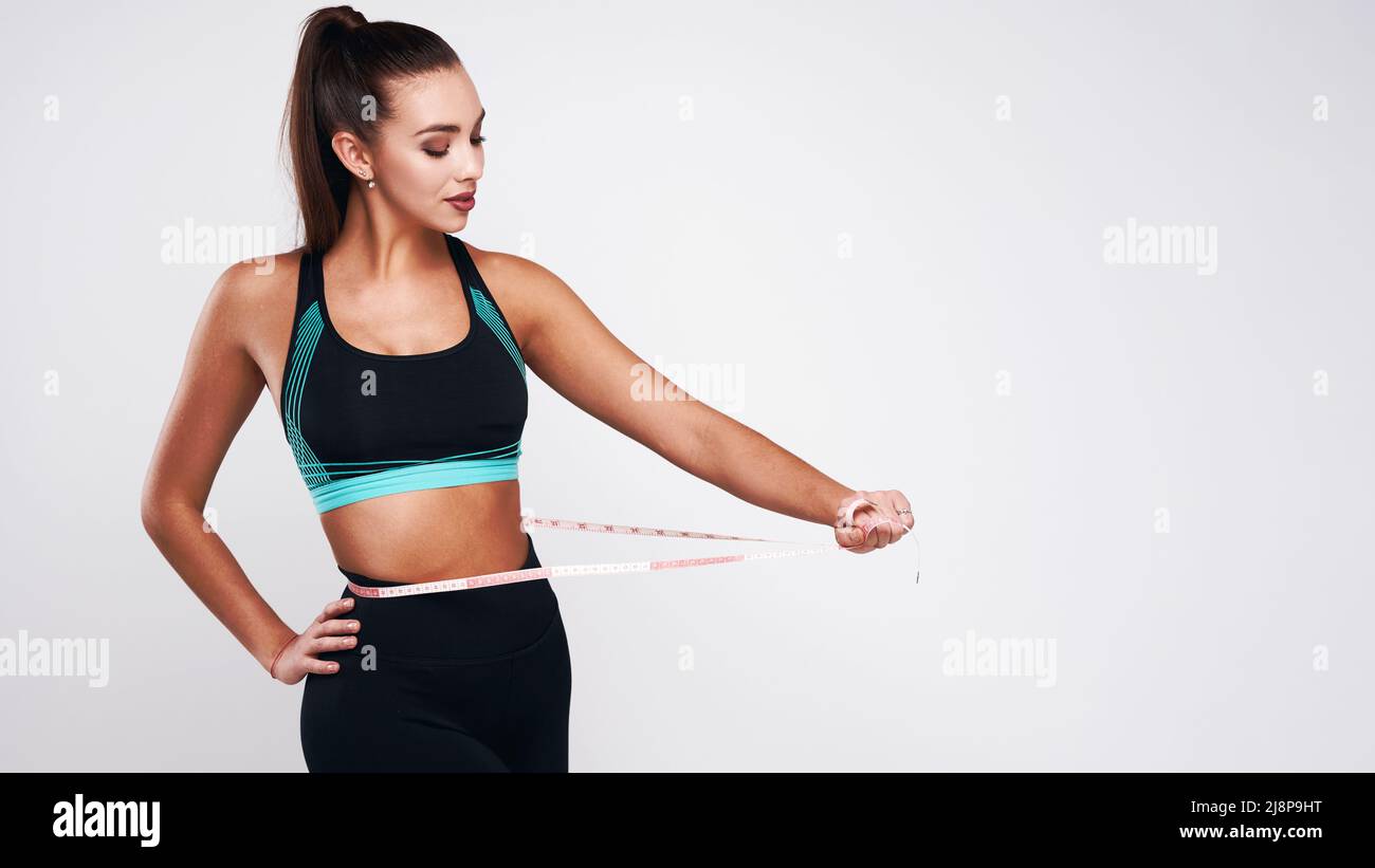 Strong white fitness female in sport suit measuring waist on gray ...