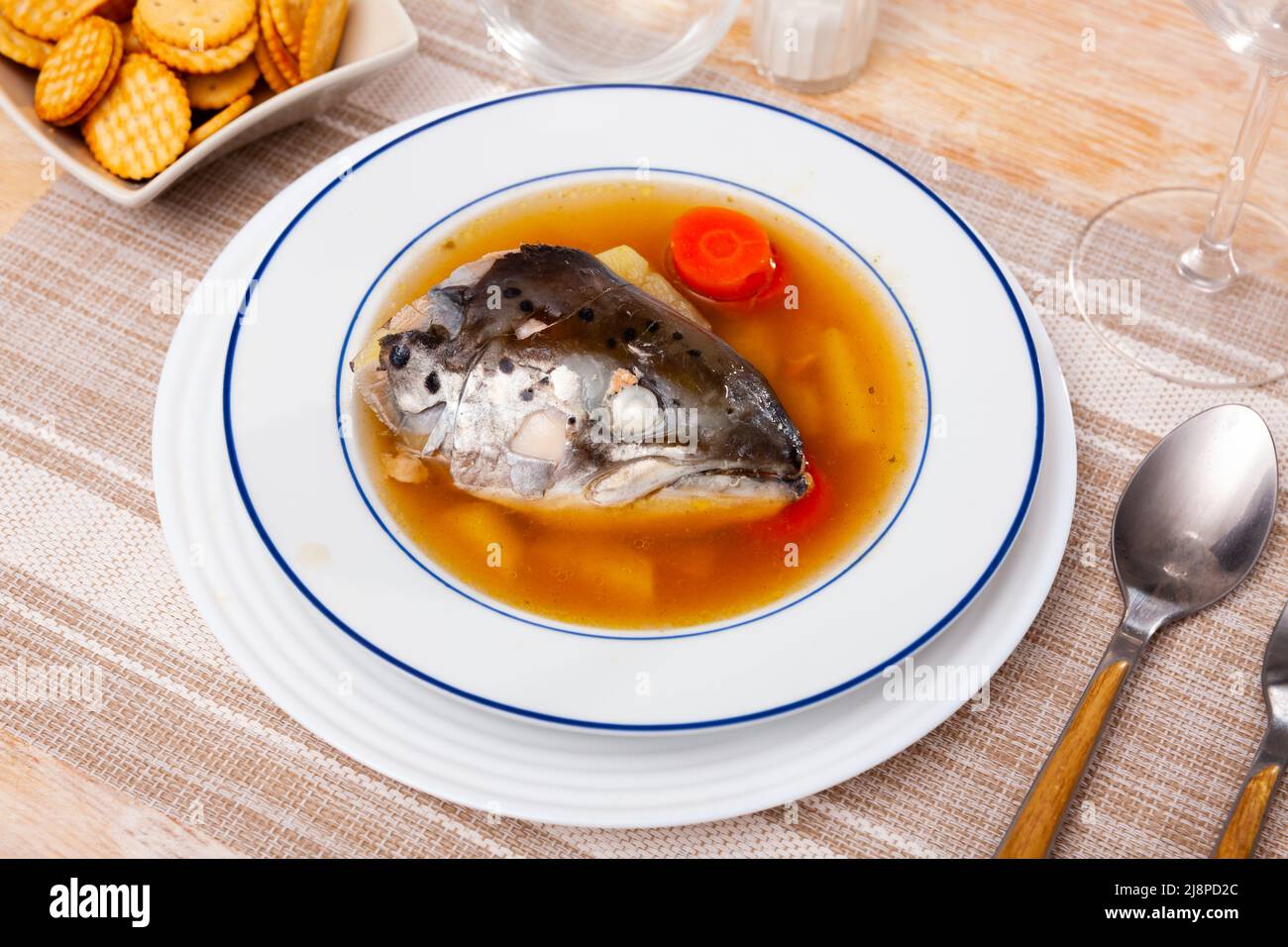 Fish broth with salmon head and vegetables served with salty crackers ...