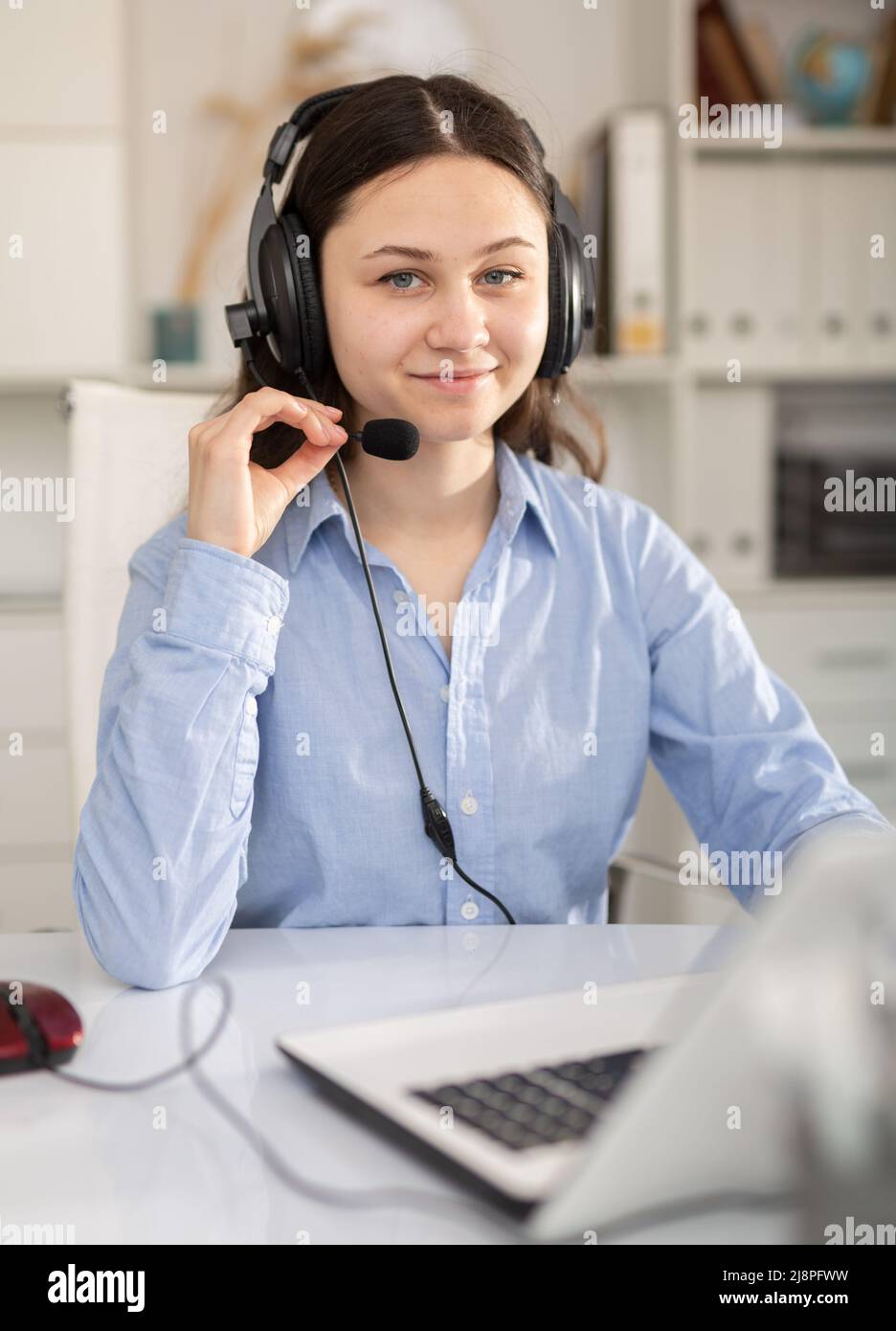 Office worker woman is working at a computer and talking by headset ...